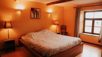 Quarto com cama de madeira, duas mesas de cabeceira com luminárias, uma cadeira, janela com cortinas e um quadro na parede.