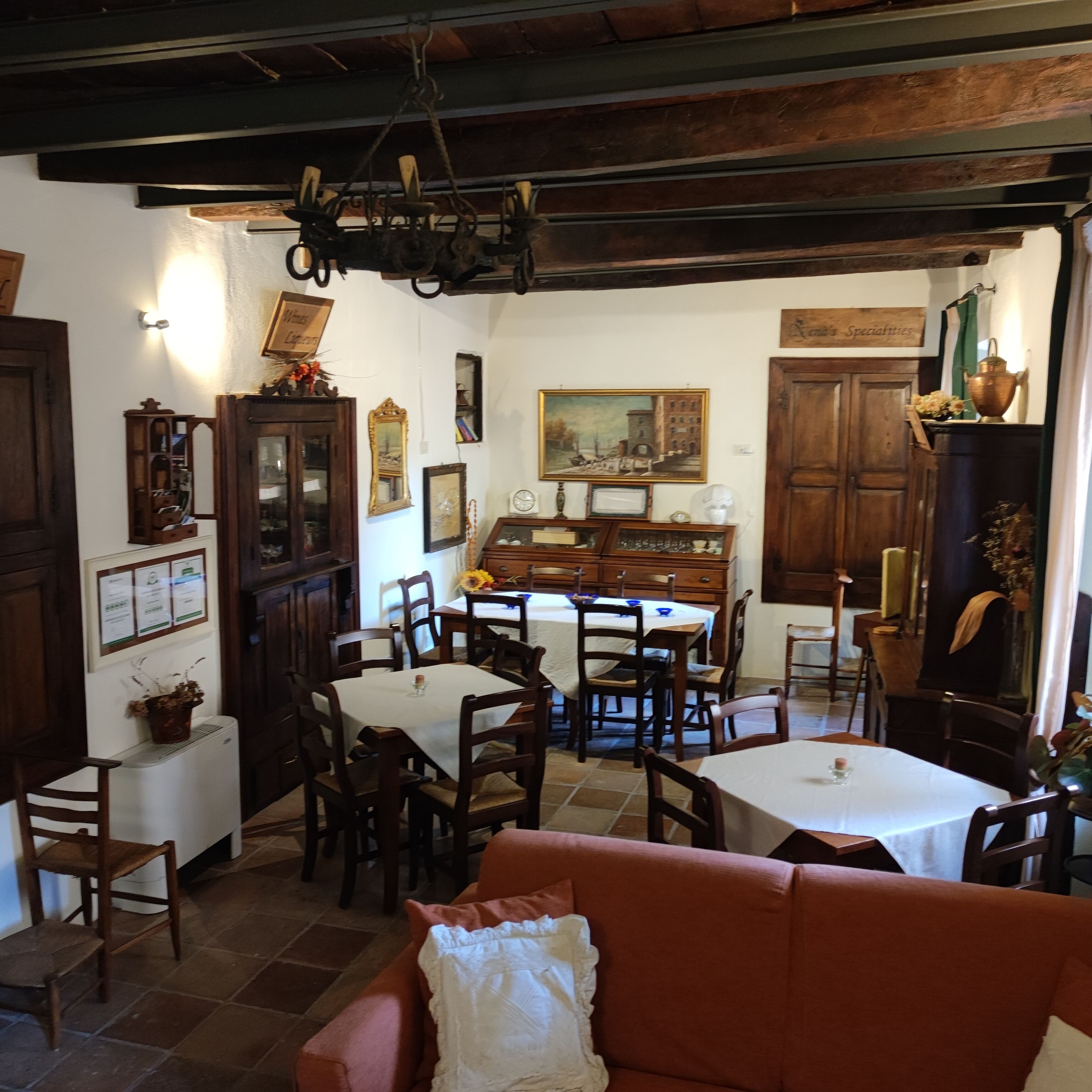 Uma área de refeições com uma mesa posta para quatro pessoas, rodeada por cadeiras de madeira. Há um sofá vermelho em primeiro plano.