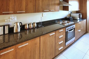 Uma cozinha moderna com armários de madeira, bancada de granito, fogão, micro-ondas e diversos eletrodomésticos.