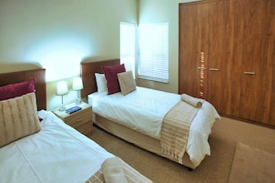 Quarto de hotel com duas camas, um guarda-roupa e uma janela com persianas.