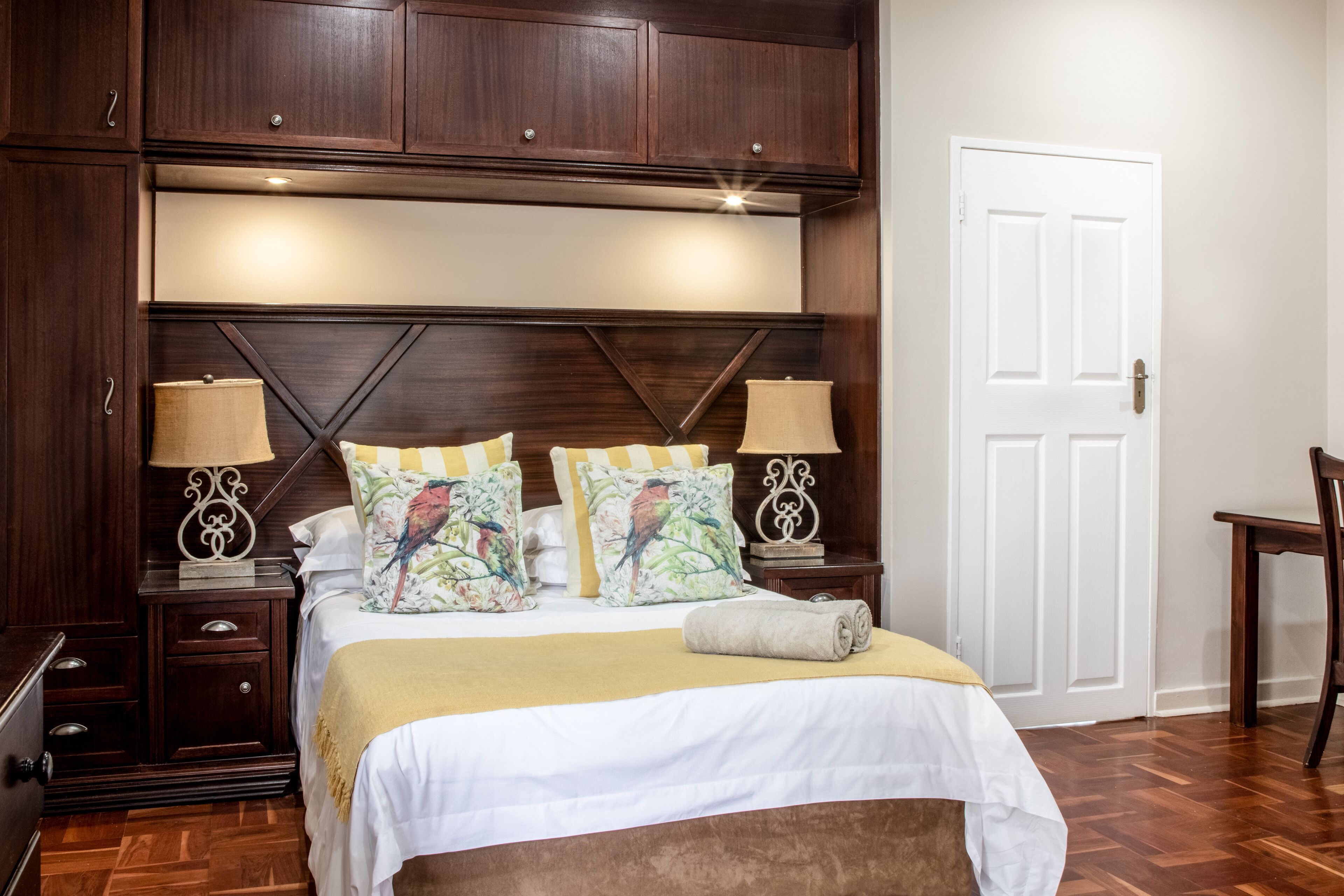 Quarto bem arrumado com uma cama grande, duas mesas de cabeceira com abajures, um guarda-roupa de madeira e uma porta.