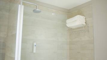 Um chuveiro com porta de vidro, um porta-toalhas com toalhas dobradas e uma garrafa branca na parede.