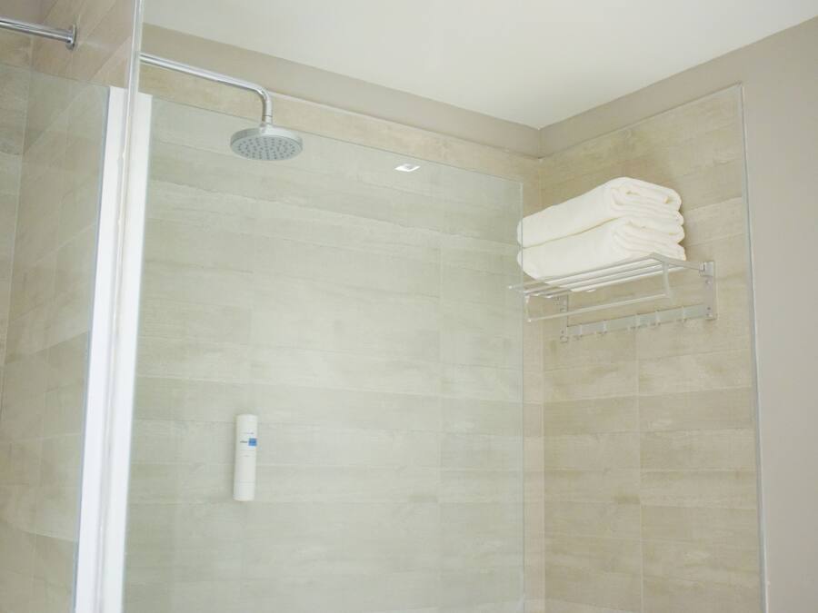 Um chuveiro com porta de vidro, um porta-toalhas com toalhas dobradas e uma garrafa branca na parede.