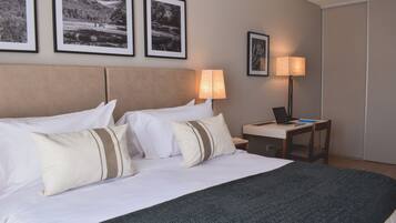 Quarto de hotel com uma cama grande, duas mesas de cabeceira, uma escrivaninha com um laptop e quadros nas paredes.