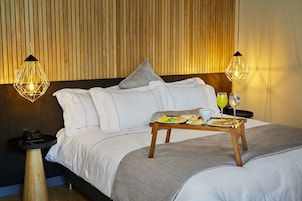 Cama bem arrumada com lençóis brancos, mesa de cabeceira com telefone e mesa auxiliar com itens de café da manhã.
