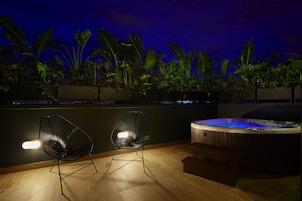 Terraço no telhado com hidromassagem, duas cadeiras e um jardim com plantas tropicais.