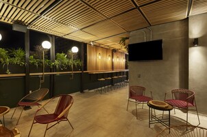 Uma área de bar moderna com teto de ripas de madeira, banquetas de bar e cadeiras vermelhas.