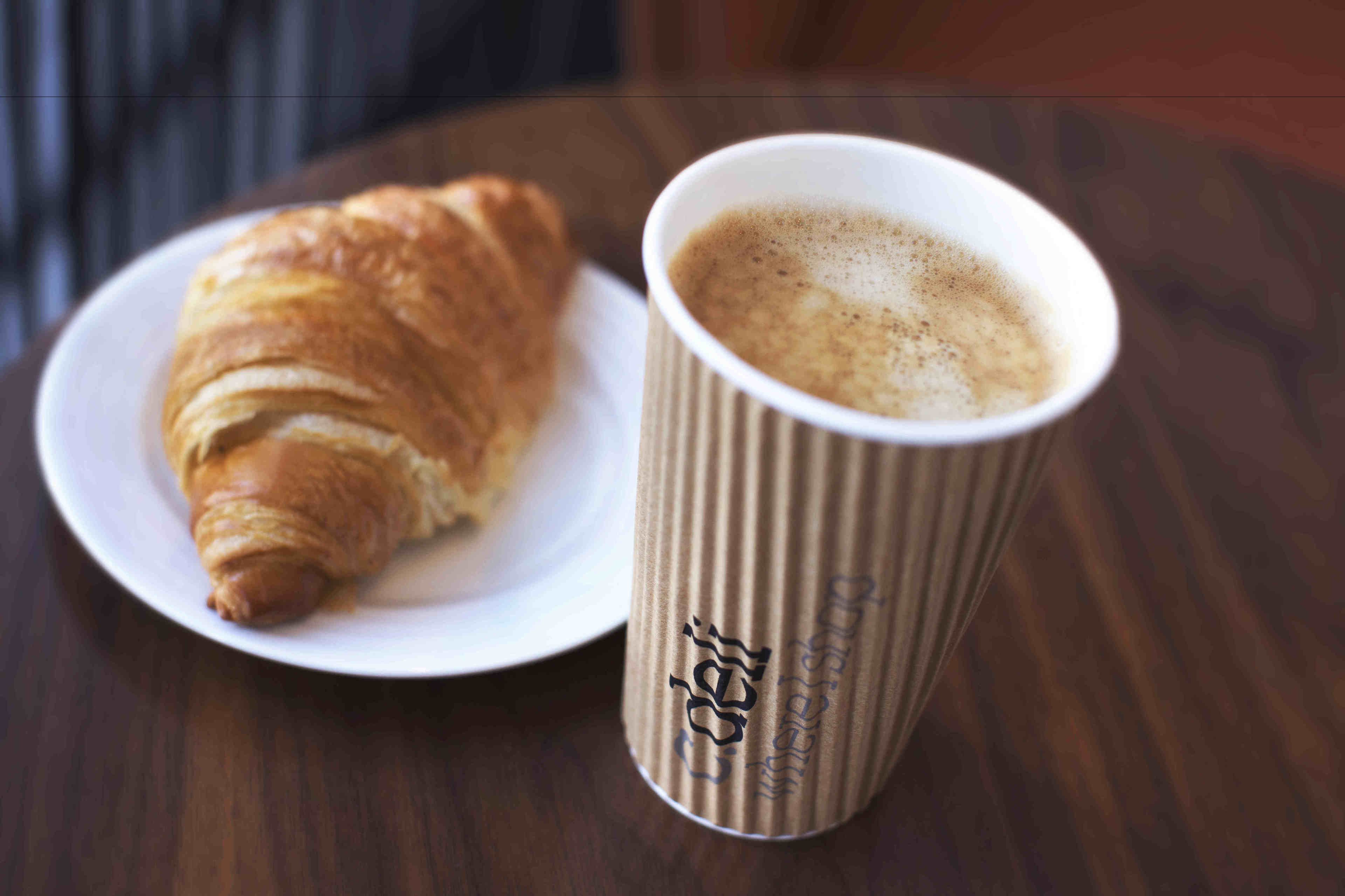 Um croissant e uma chávena de café sobre uma mesa de madeira.