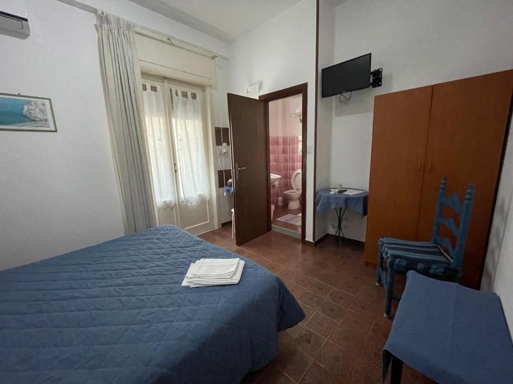 Quarto com cama, escrivaninha, cadeira, televisão e guarda-roupa.