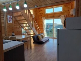 Interior de uma cabana de madeira com área de jantar, sofá e escada.