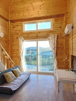 Interior de uma cabana de madeira com sofá, mesa e janela com cortinas.