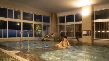 Piscina interna com água cristalina, grandes janelas e um pilar de pedra.