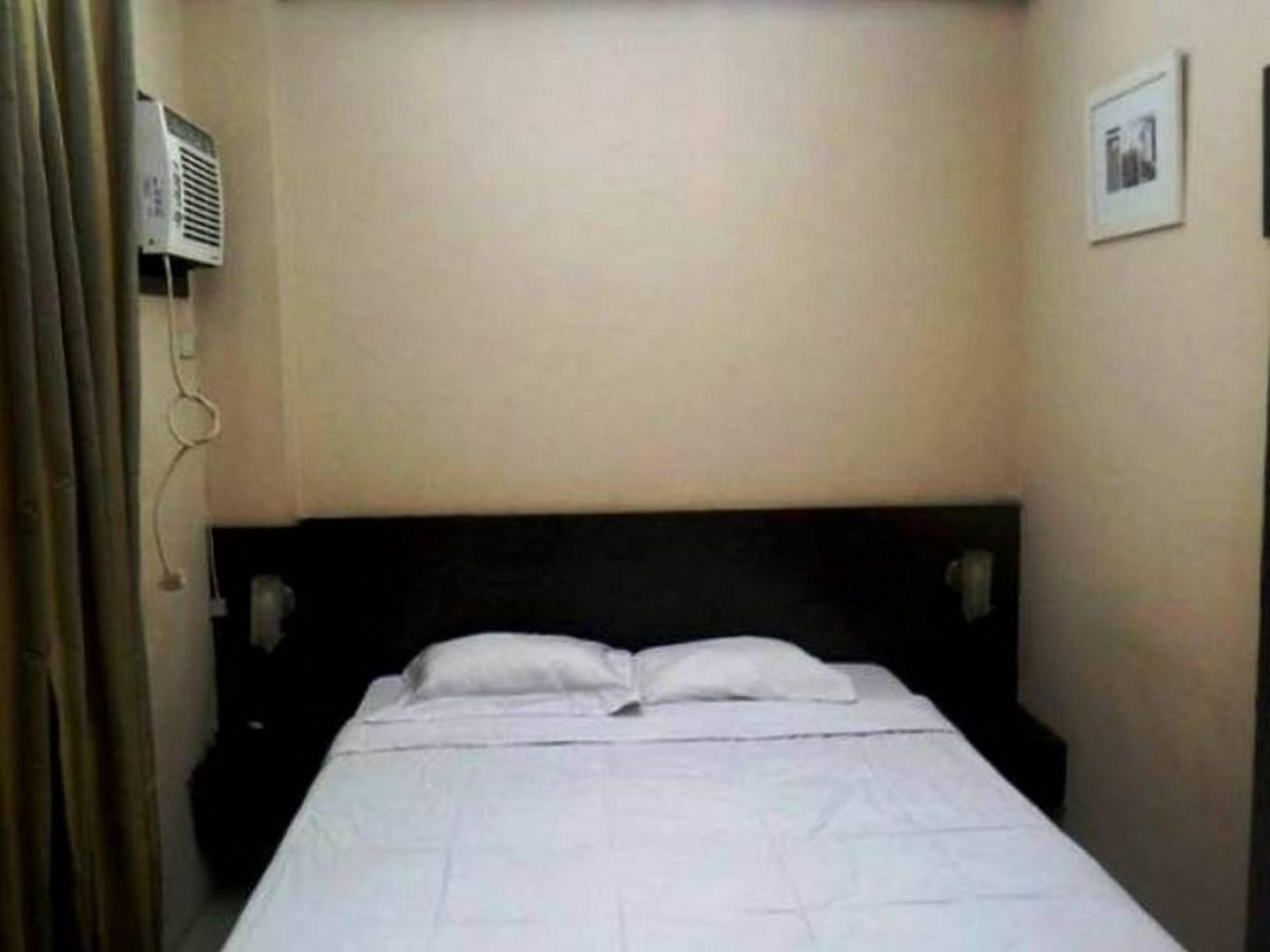 Quarto de hotel com uma cama, mesa de cabeceira, ar condicionado e quadro na parede.
