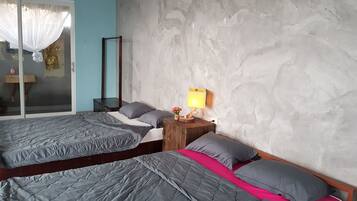 Quarto com duas camas, uma mesa de cabeceira com abajur, um espelho e uma porta deslizante com cortina translúcida.