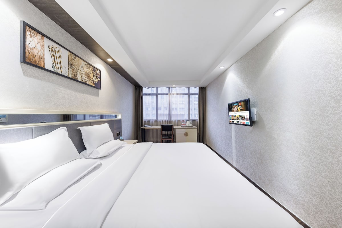 Quarto de hotel moderno com uma cama grande, uma mesa de trabalho e uma televisão.