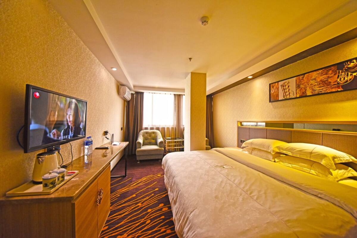 Quarto de hotel com cama, televisão, escrivaninha, cadeira e janela.