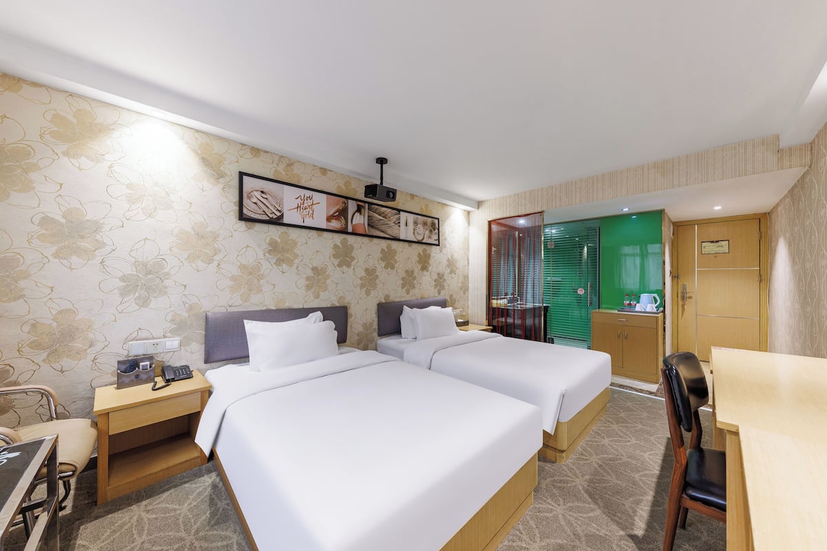 Quarto de hotel com duas camas, uma escrivaninha, uma cadeira, um guarda-roupa e uma porta verde.
