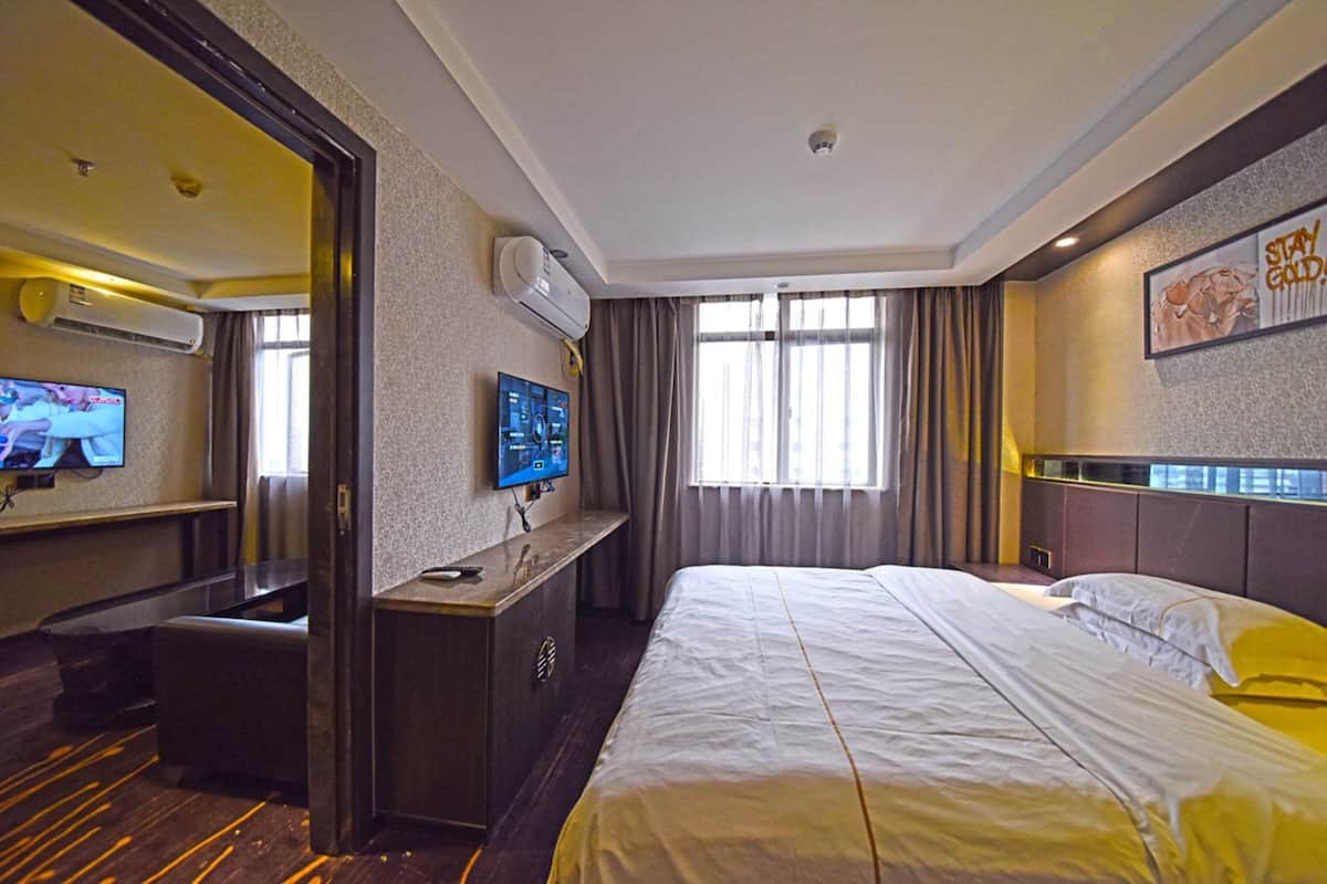 Quarto de hotel com cama, escrivaninha, televisão e janela com cortinas.