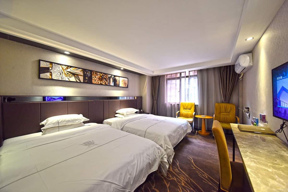 Quarto de hotel com duas camas, uma mesa pequena, uma poltrona amarela, uma televisão e uma obra de arte na parede.
