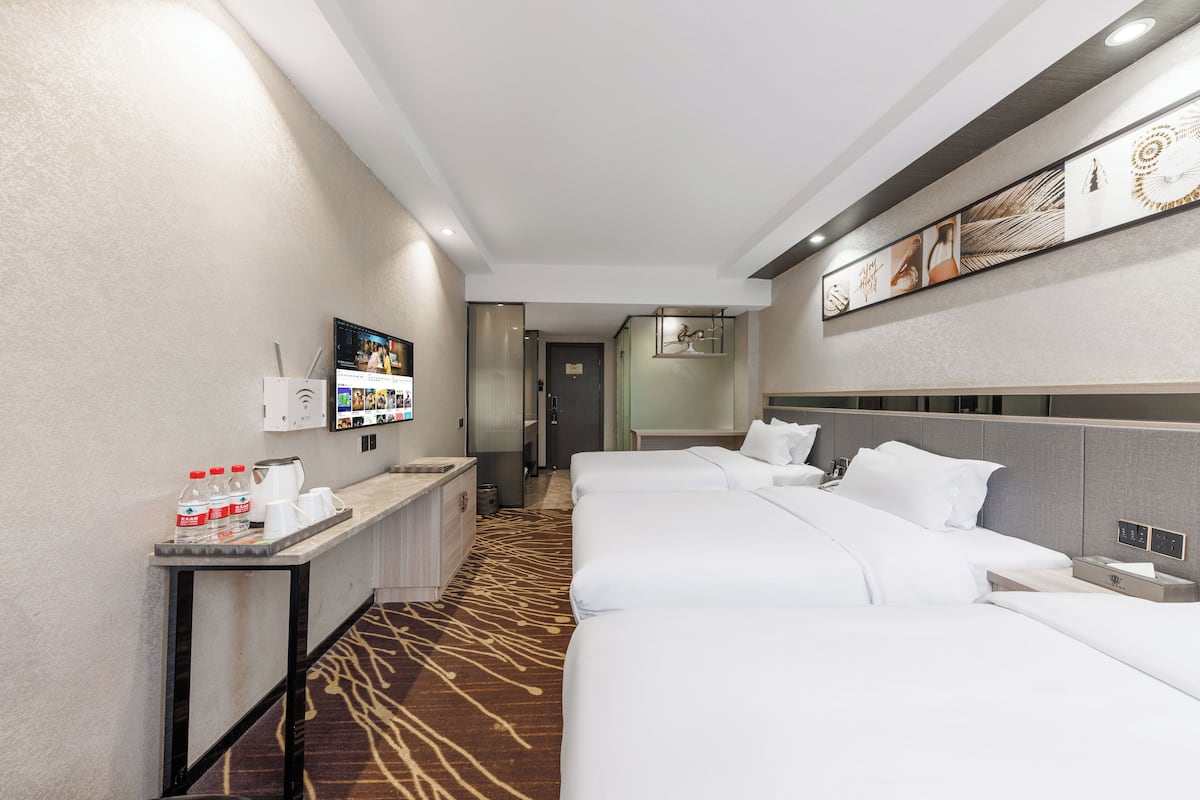 Quarto de hotel com duas camas, uma secretária pequena com cafeteira e uma televisão na parede.