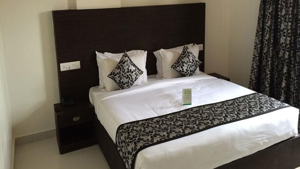 Uma cama bem arrumada com cabeceira escura, roupa de cama branca e duas almofadas estampadas.