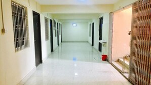 Um corredor comprido e estreito, com portas em ambos os lados, piso de azulejos e um balde vermelho no final da direita.