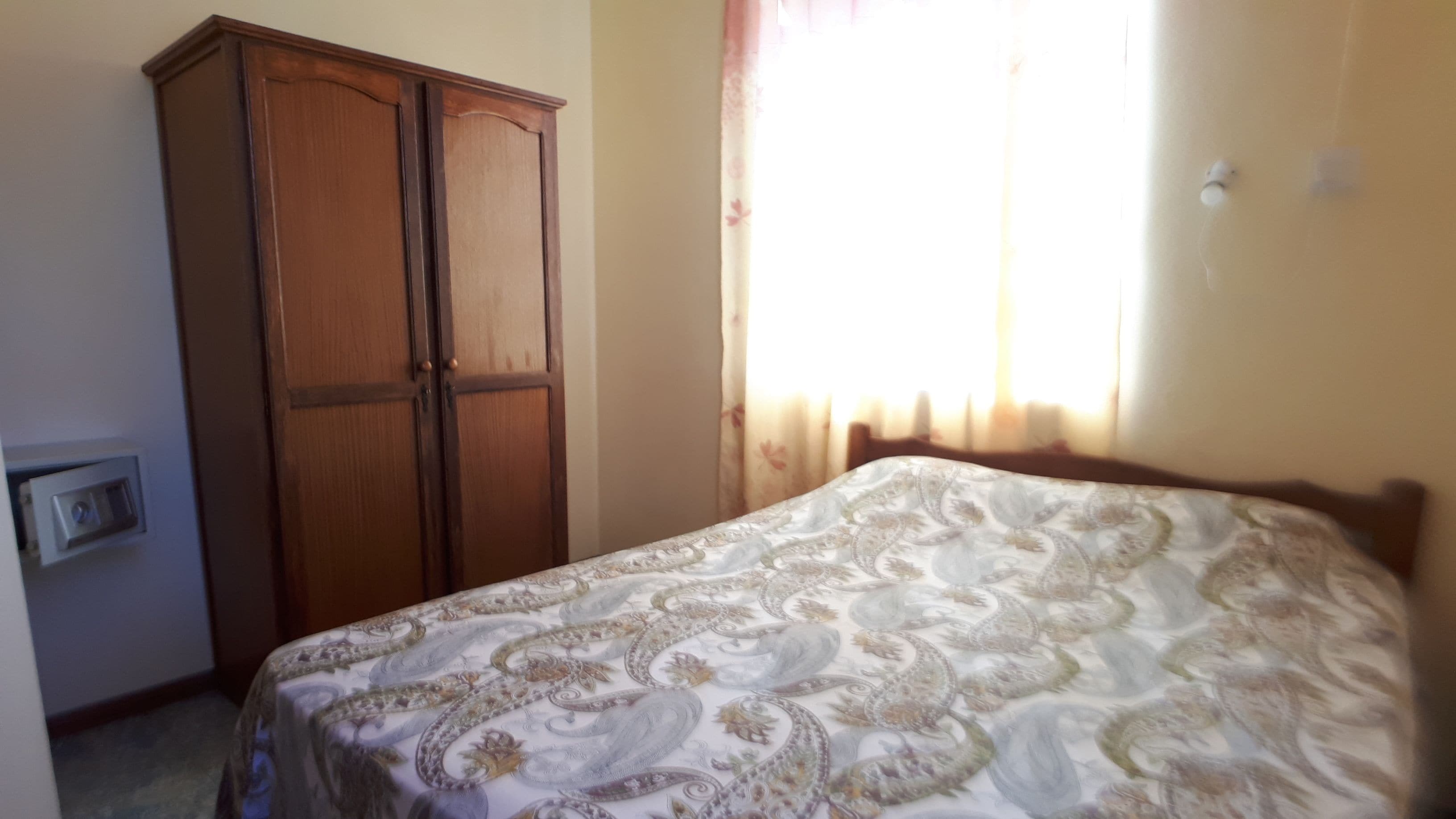 Um quarto com uma cama, um guarda-roupa e uma janela com cortinas.