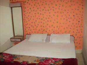 Quarto com cama, duas almofadas, mesa de cabeceira, espelho e papel de parede com padrão floral.