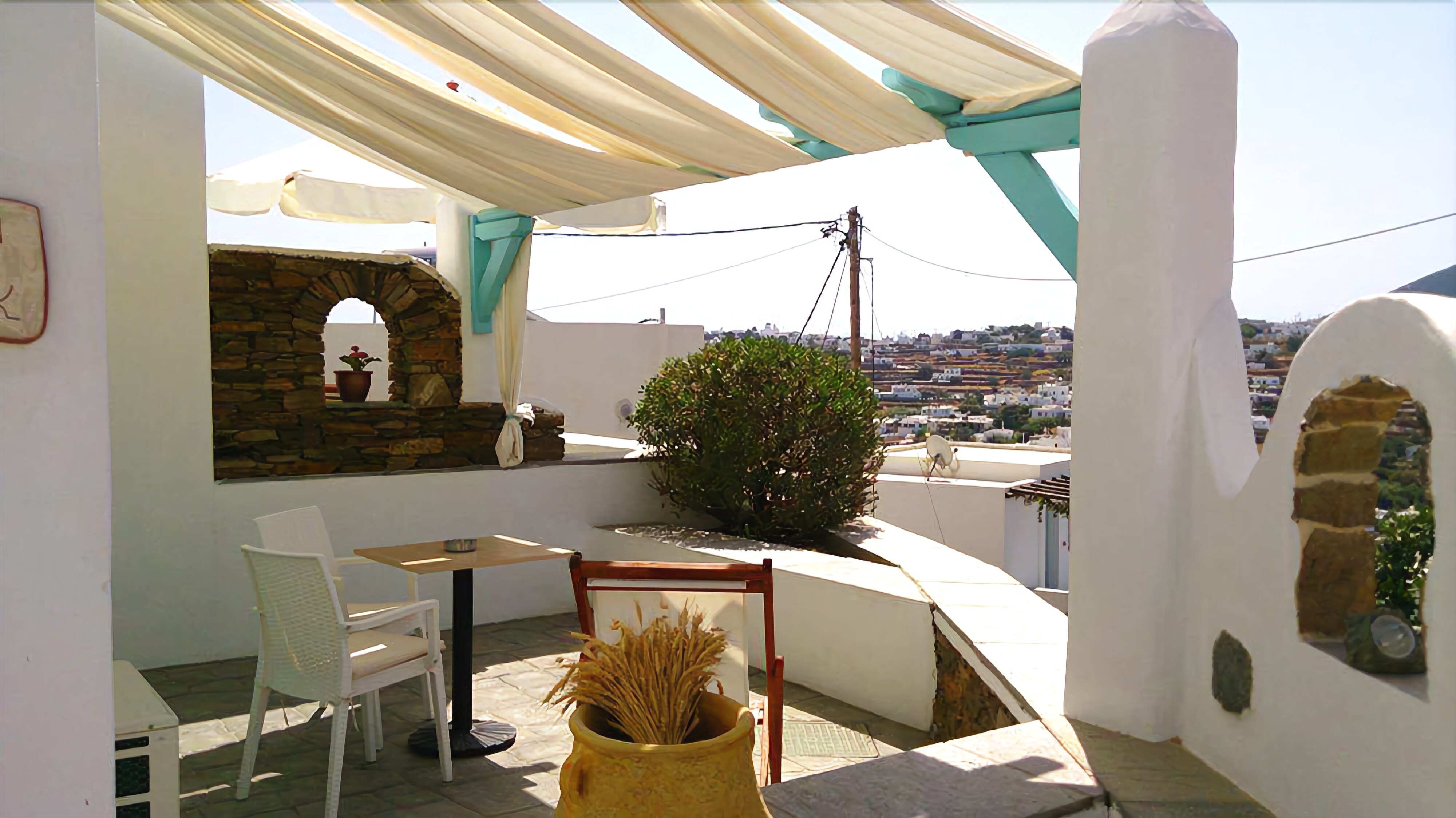 Um terraço com mesa e cadeiras, um vaso de planta e vista para a cidade.