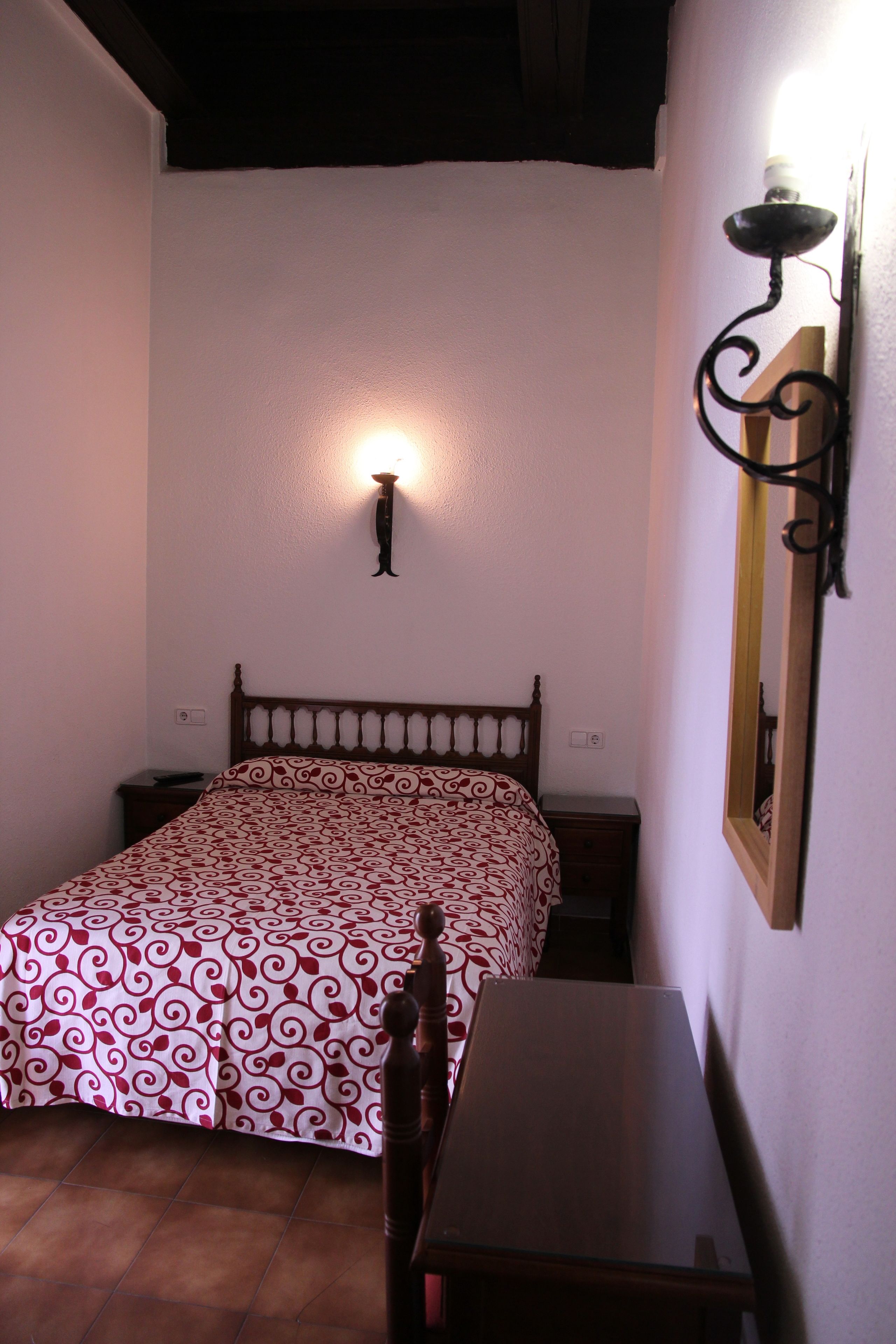 Um quarto pequeno e acolhedor com uma cama, mesa de cabeceira e luminária na parede.