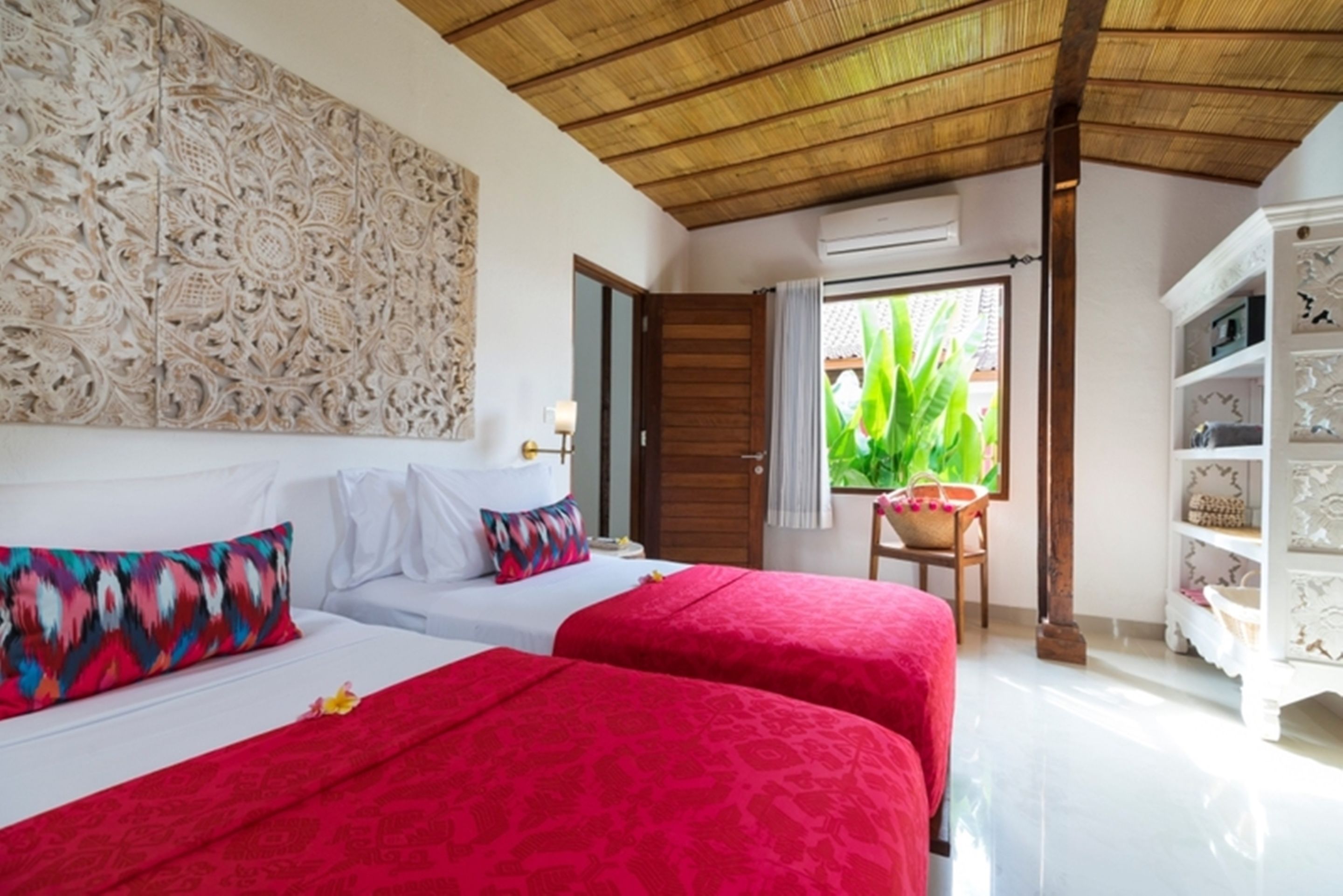 Quarto de hotel com duas camas, uma parede decorativa grande, teto de madeira e vista para o verde lá fora.