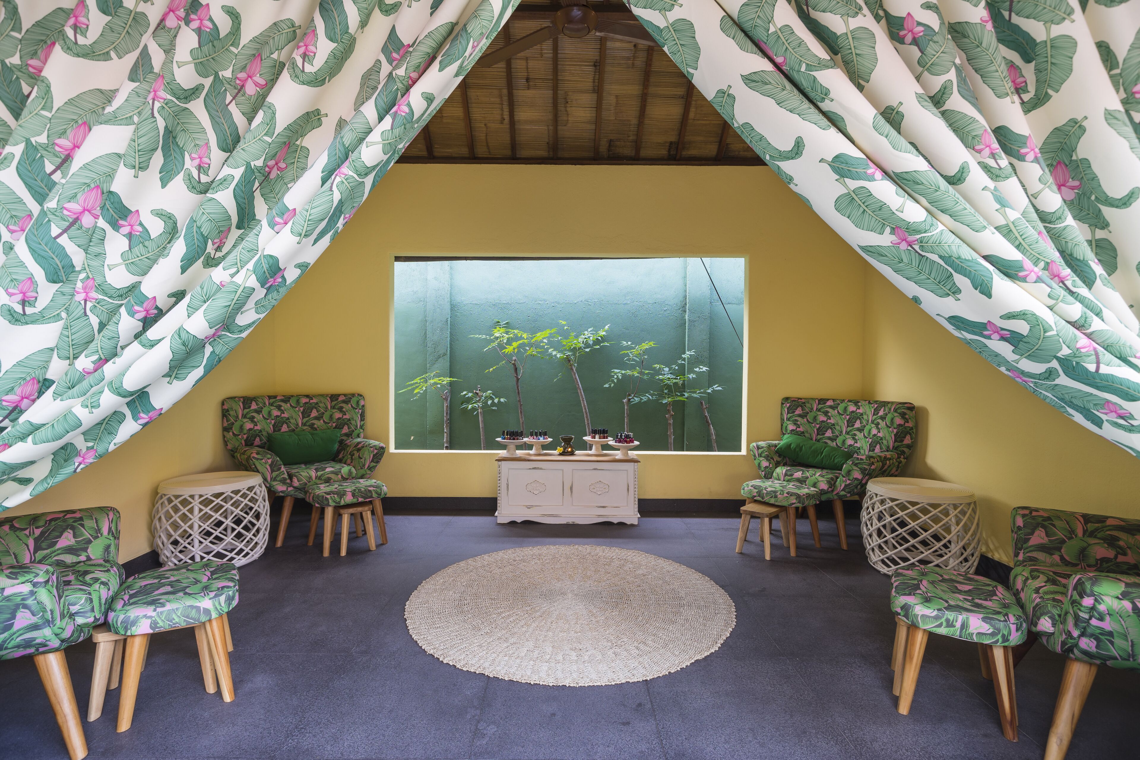 Um quarto acolhedor com uma grande janela, um tapete redondo e quatro cadeiras com estampa de folha tropical.