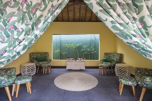 Um quarto acolhedor com uma grande janela, um tapete redondo e quatro cadeiras com estampa de folha tropical.