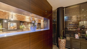 Uma área de recepção moderna com painéis de madeira, uma vitrine de vidro e um vaso com planta.