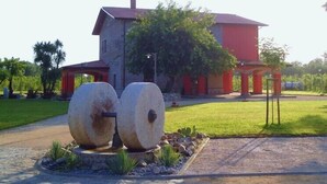 Um edifício com fachada em vermelho e cinza, duas grandes estruturas cilíndricas em primeiro plano e um gramado bem cuidado.