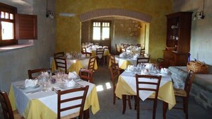 Uma sala de jantar com mesas preparadas para vários convidados, cadeiras de madeira e decoração rústica com vigas aparentes e parede amarela.