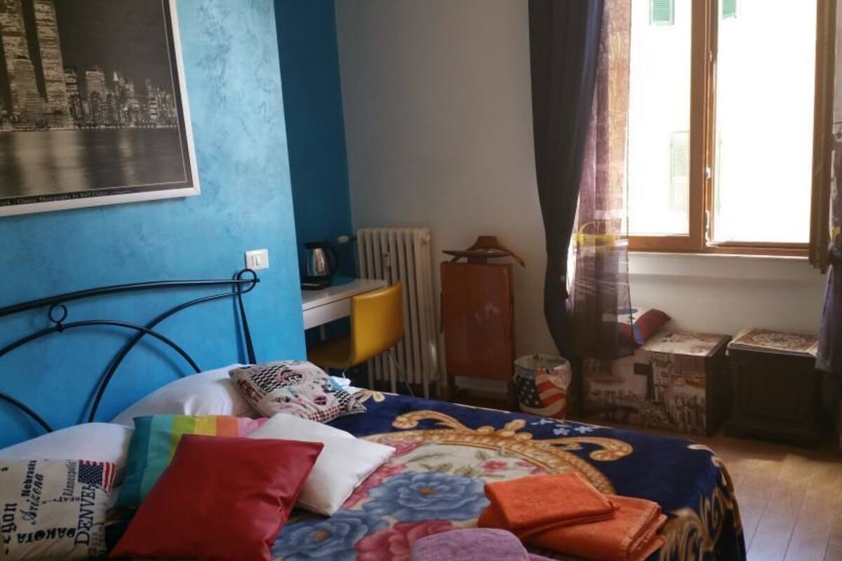 Quarto com cama, radiador, janela com cortinas e uma cadeira.