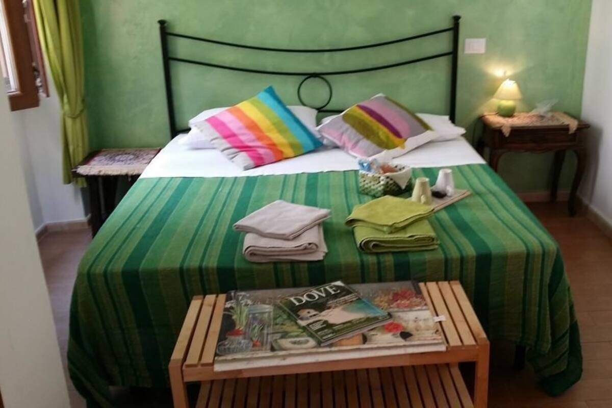 Quarto com uma cama, mesa de cabeceira, pequena mesa com revistas e uma luminária.