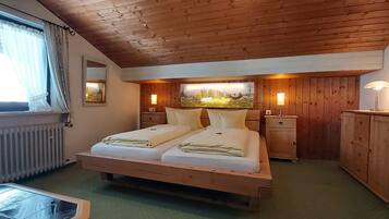 Quarto aconchegante com cama de madeira, duas mesas de cabeceira com luminárias, um radiador e uma janela grande com cortinas.