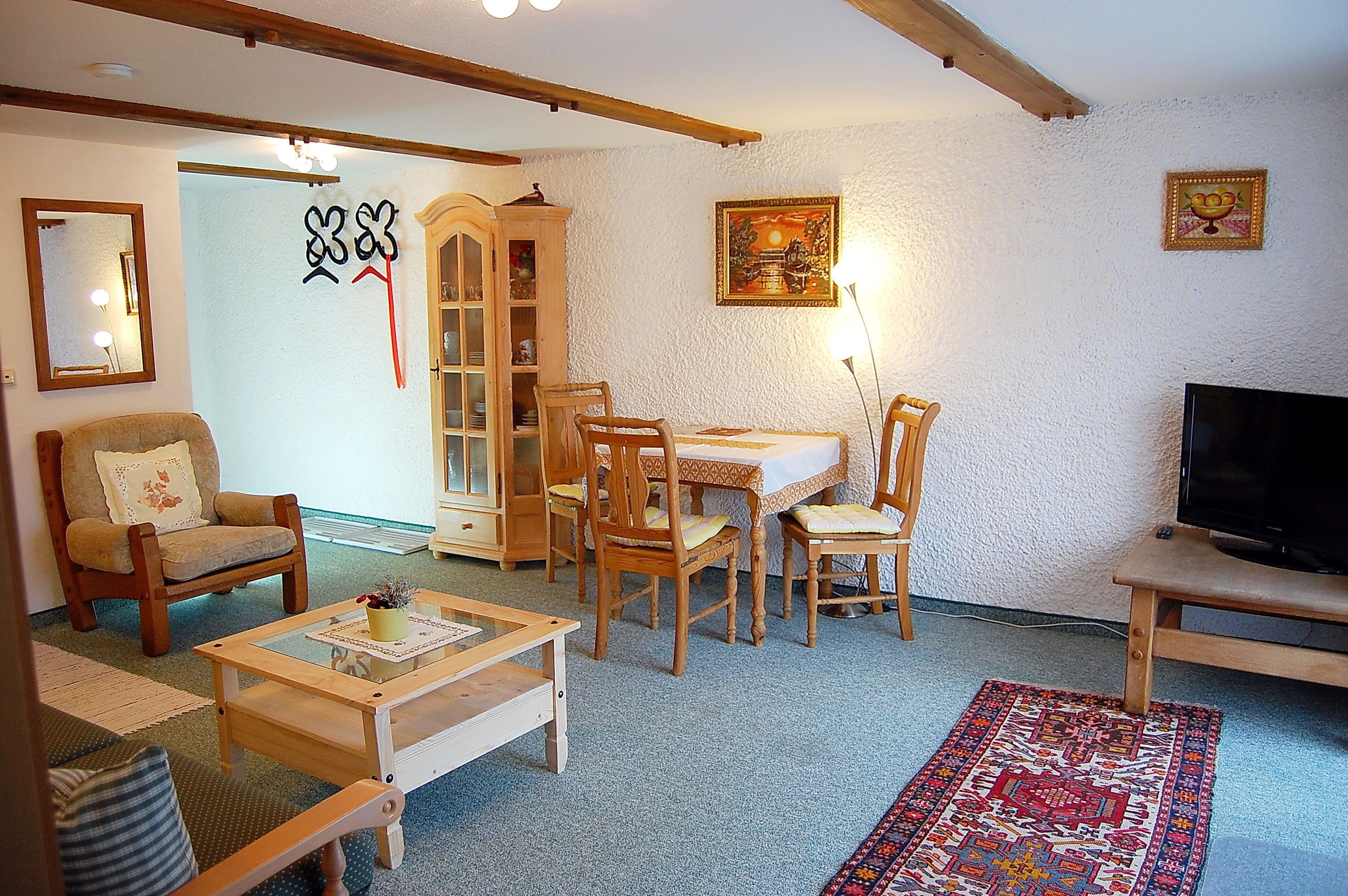 Uma sala de estar aconchegante com uma mesa de centro de madeira, uma mesa de jantar com cadeiras, uma televisão e uma estante de livros.