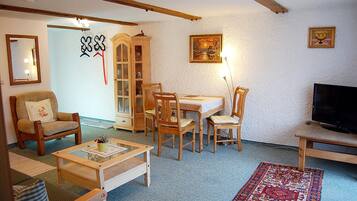 Uma sala de estar aconchegante com uma mesa de centro de madeira, uma mesa de jantar com cadeiras, uma televisão e uma estante de livros.