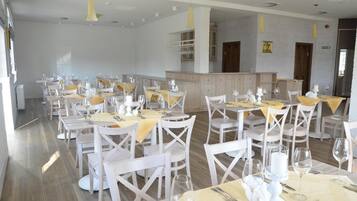 Uma sala de jantar com cadeiras e mesas brancas, toalhas de mesa amarelas e luminárias pendentes.