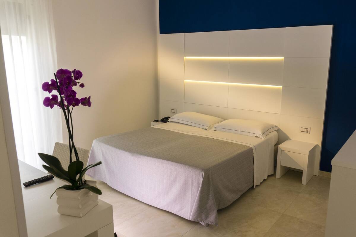 Quarto moderno com cama, mesas de cabeceira, um vaso de orquídea e um controle remoto no chão.
