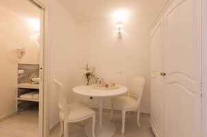 Um quarto pequeno com paredes brancas, uma mesa redonda e duas cadeiras, uma porta branca e um ponto de luz fixado na parede.