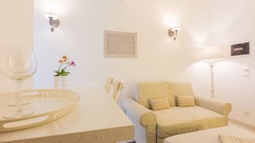 Uma sala de estar moderna com um sofá bege, uma mesinha com uma taça de vinho e luminárias decorativas na parede.