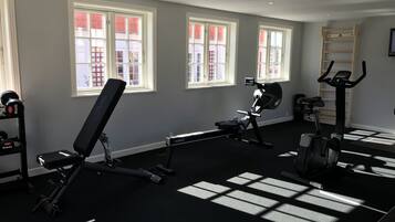 Academia com equipamentos de exercício, amplas janelas e carpete preto.