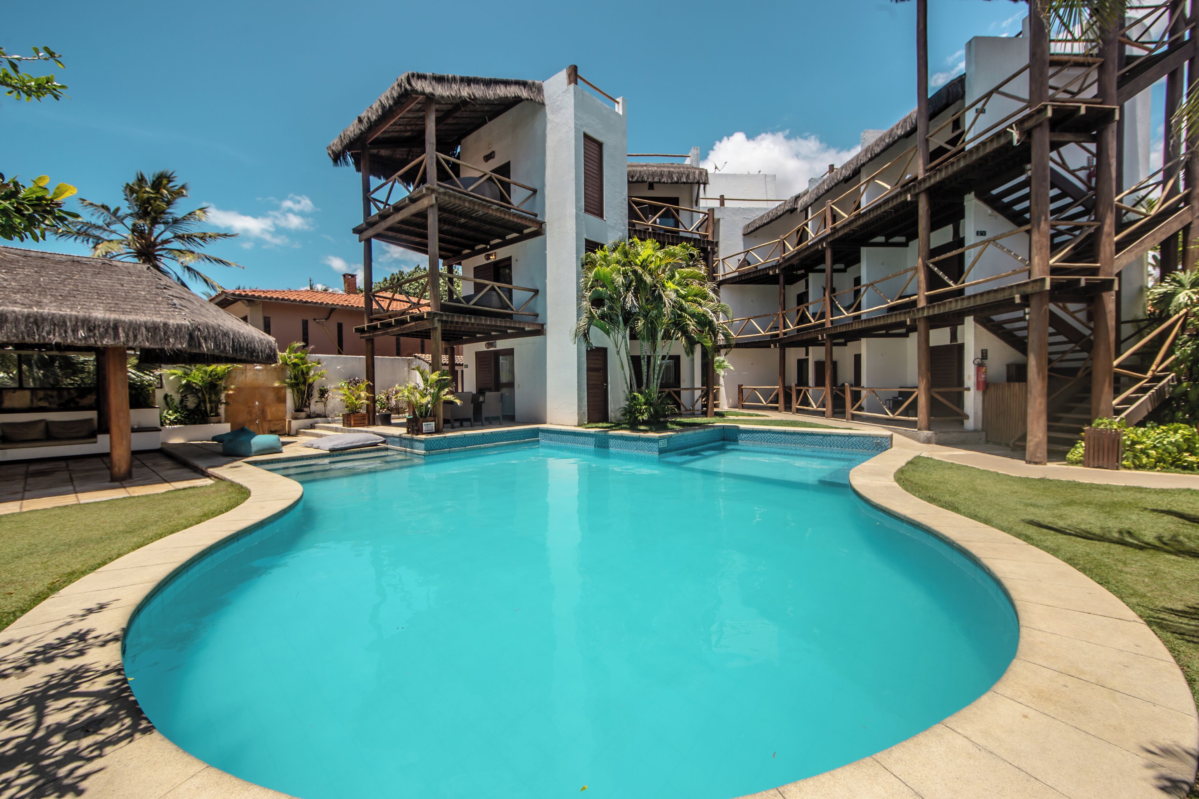 Piscina rodeada por um deck de madeira e um edifício com telhado de palha.