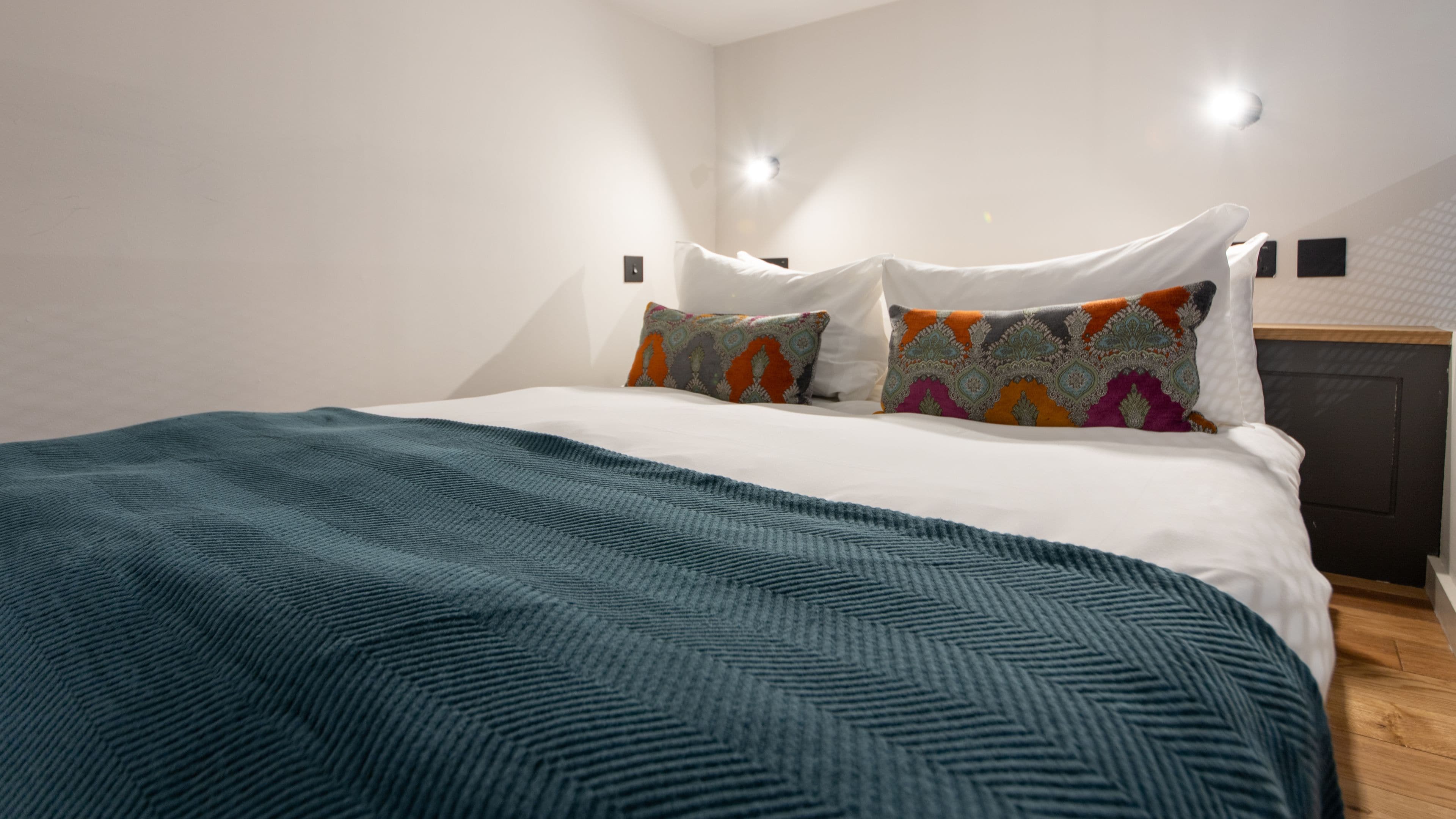 Quarto moderno com cama grande, manta estampada em tons de verde-água e duas almofadas decorativas.