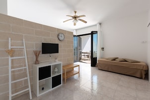 Uma sala de estar moderna com televisão de tela plana, um banco de madeira, uma estante branca, um ventilador de teto e um sofá bege.