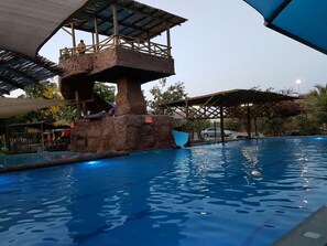 Piscina com estrutura rochosa e área de estar coberta.